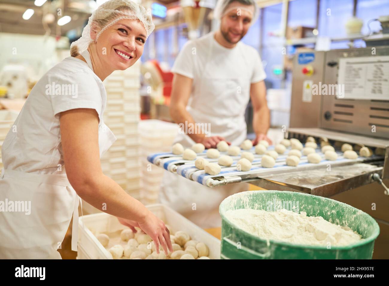 Young baker team bakes buns on the belt proofer in the family bakery ...