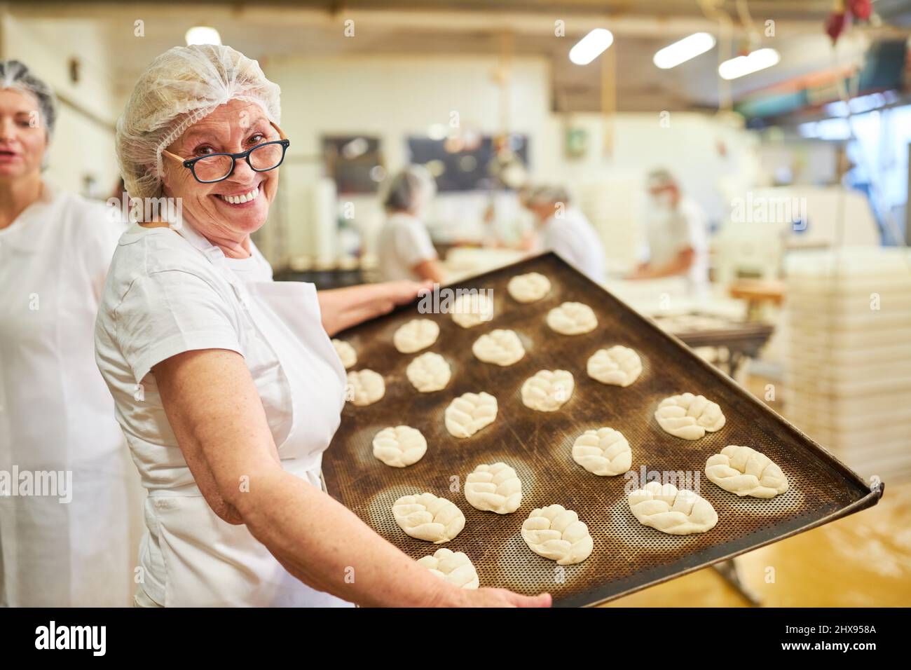 Senior woman baker with experience carries yeast braids on a baking ...
