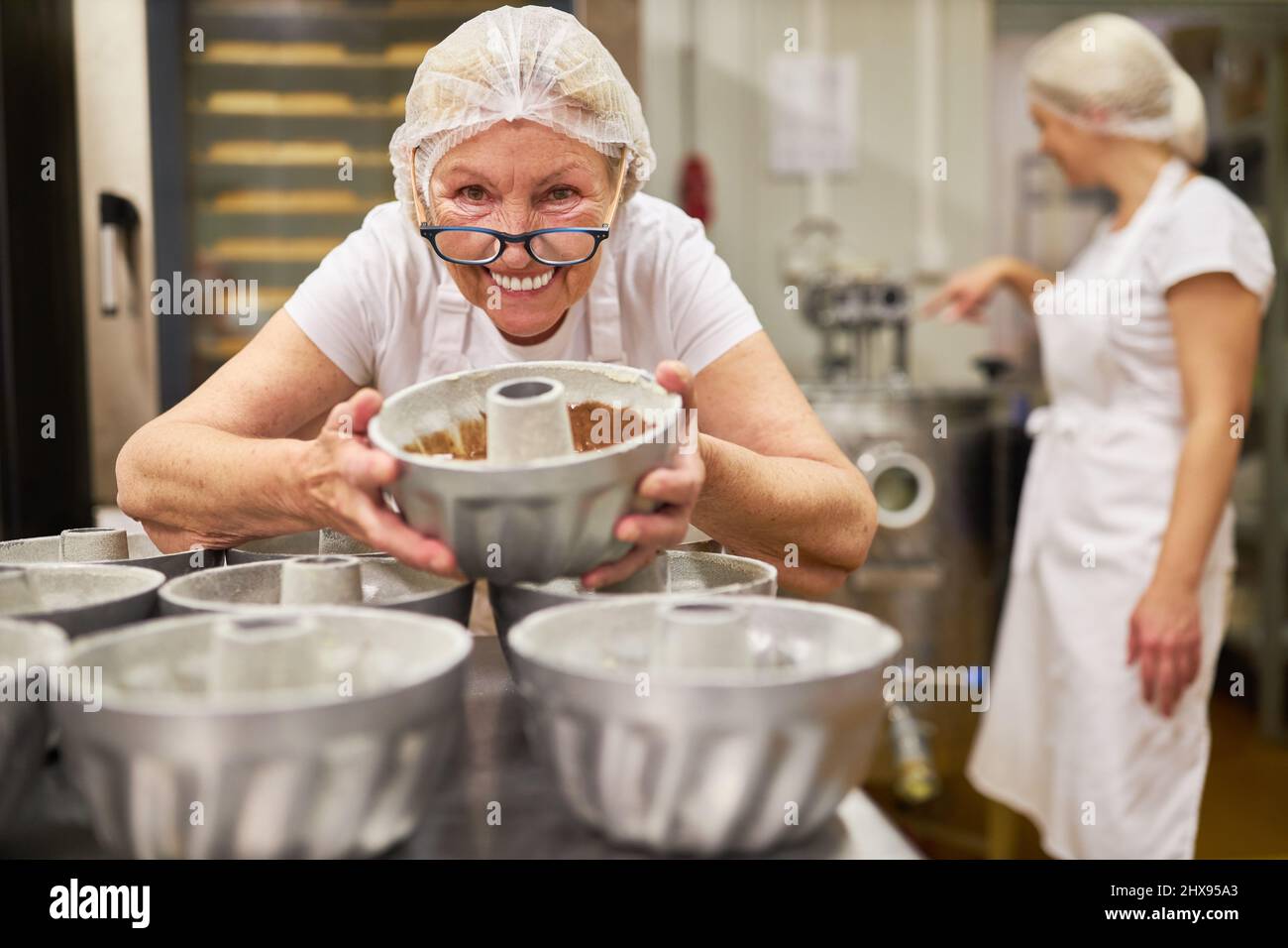 Senior woman as a baker with experience proudly shows a Gugelhupf cake ...