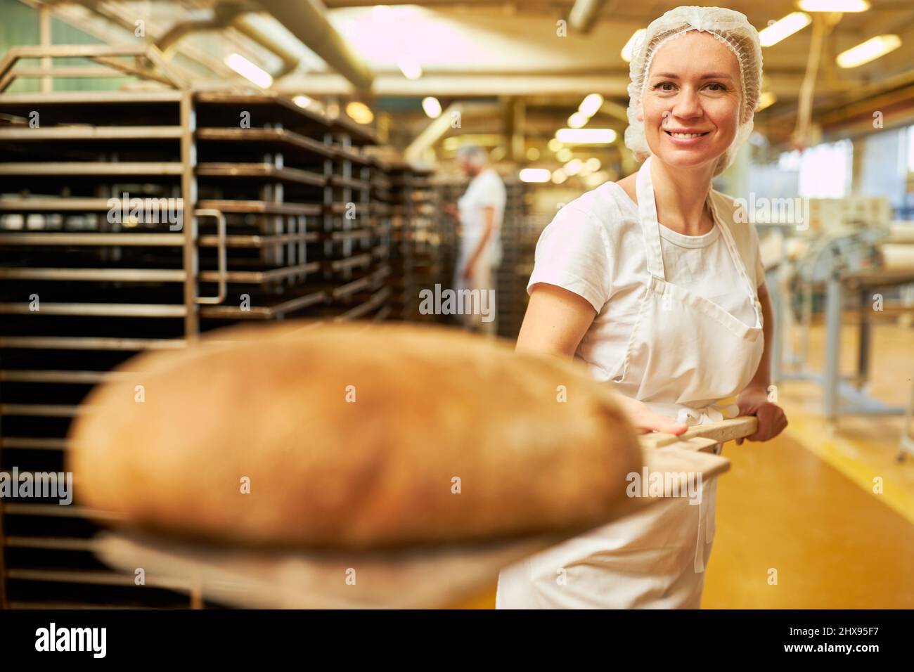 Young woman as a baker apprentice holds a bread shovel with a ready ...