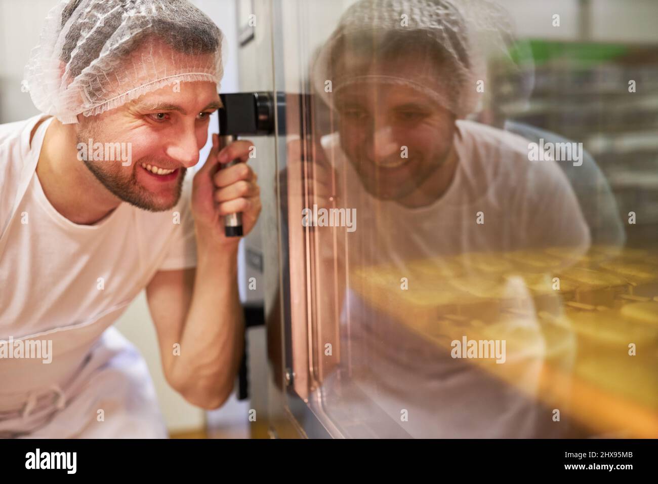 Young man as a baker's apprentice controls the baking of baked goods in ...
