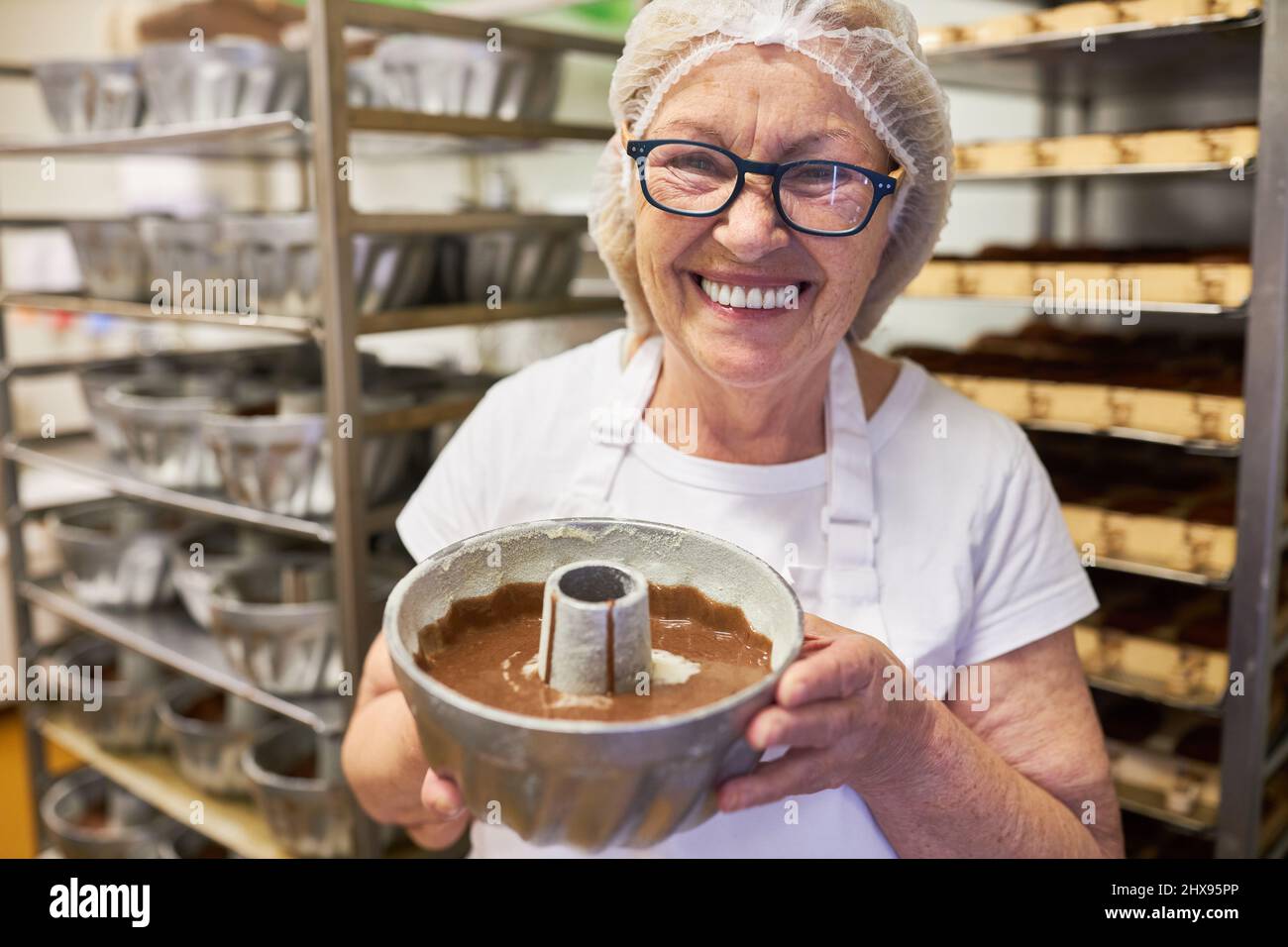 Senior woman as a baker with experience proudly shows a Gugelhupf cake ...