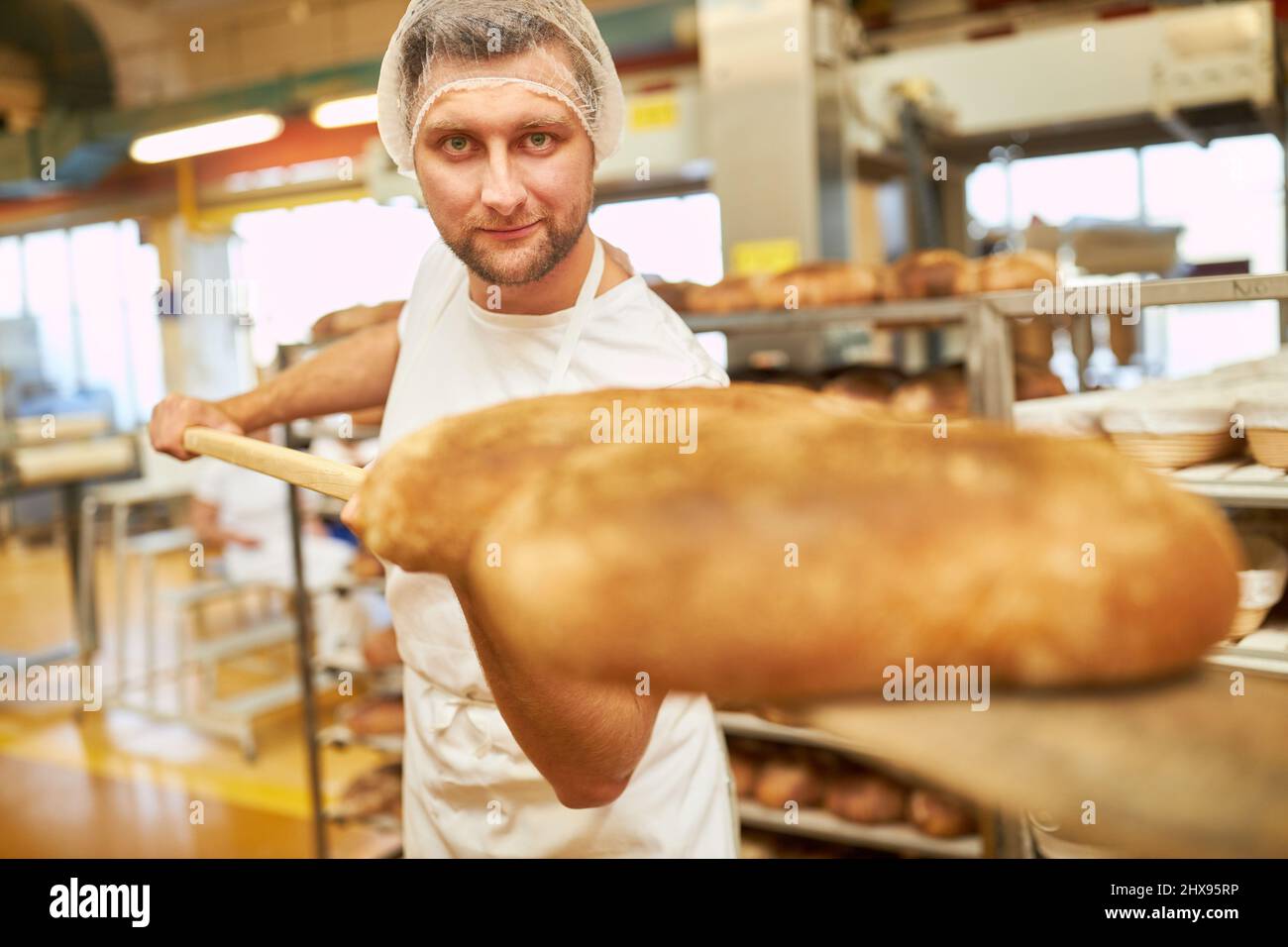 Baker apprentice holding a bread pusher with ready baked bread in the ...