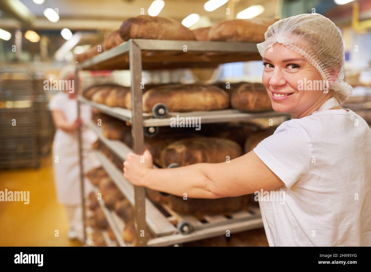 Young woman as a baker's apprentice pushes tray trolley with ready ...
