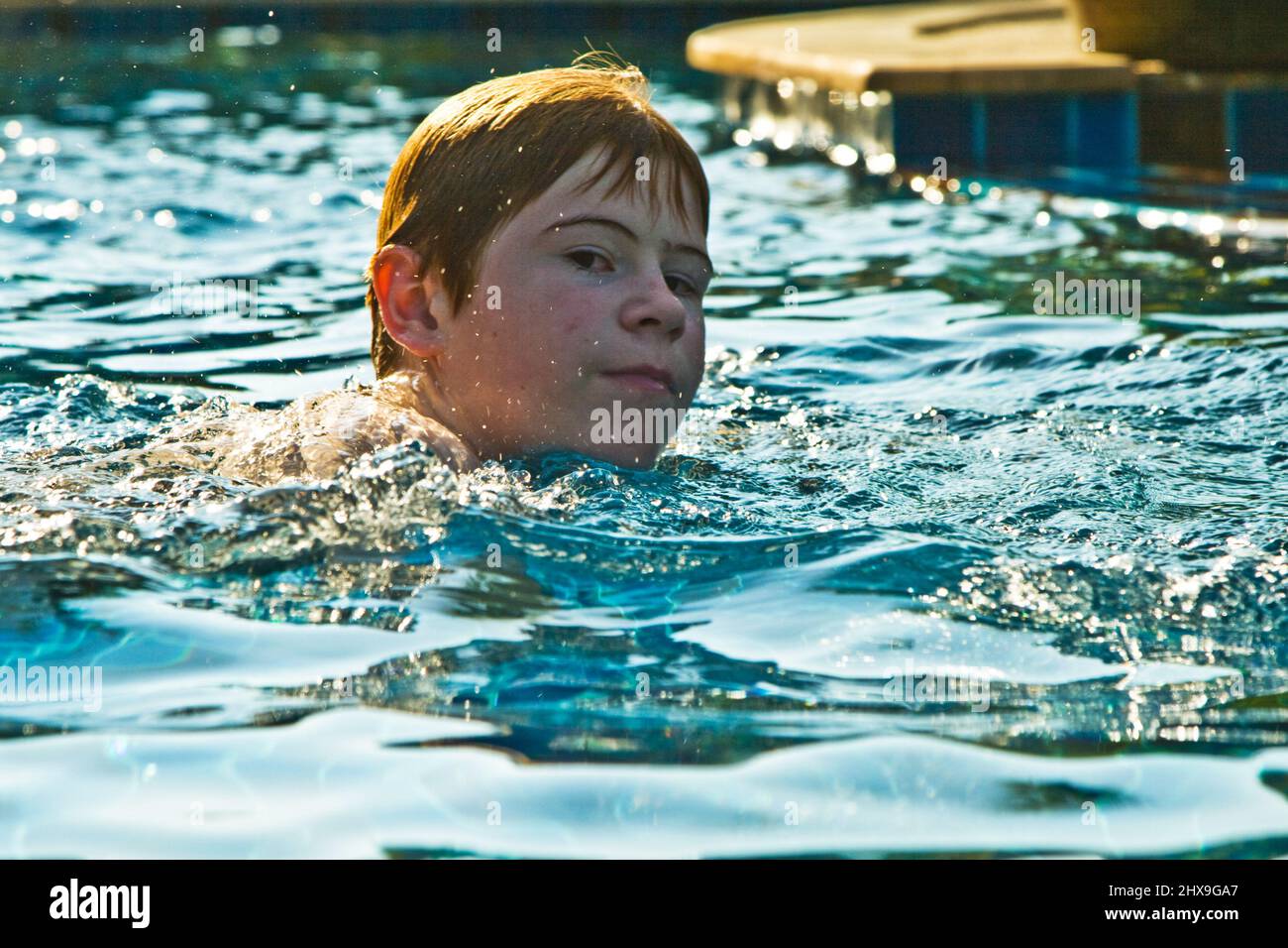 boy with red hair is swimming in the pool and enjoys the fresh water ...