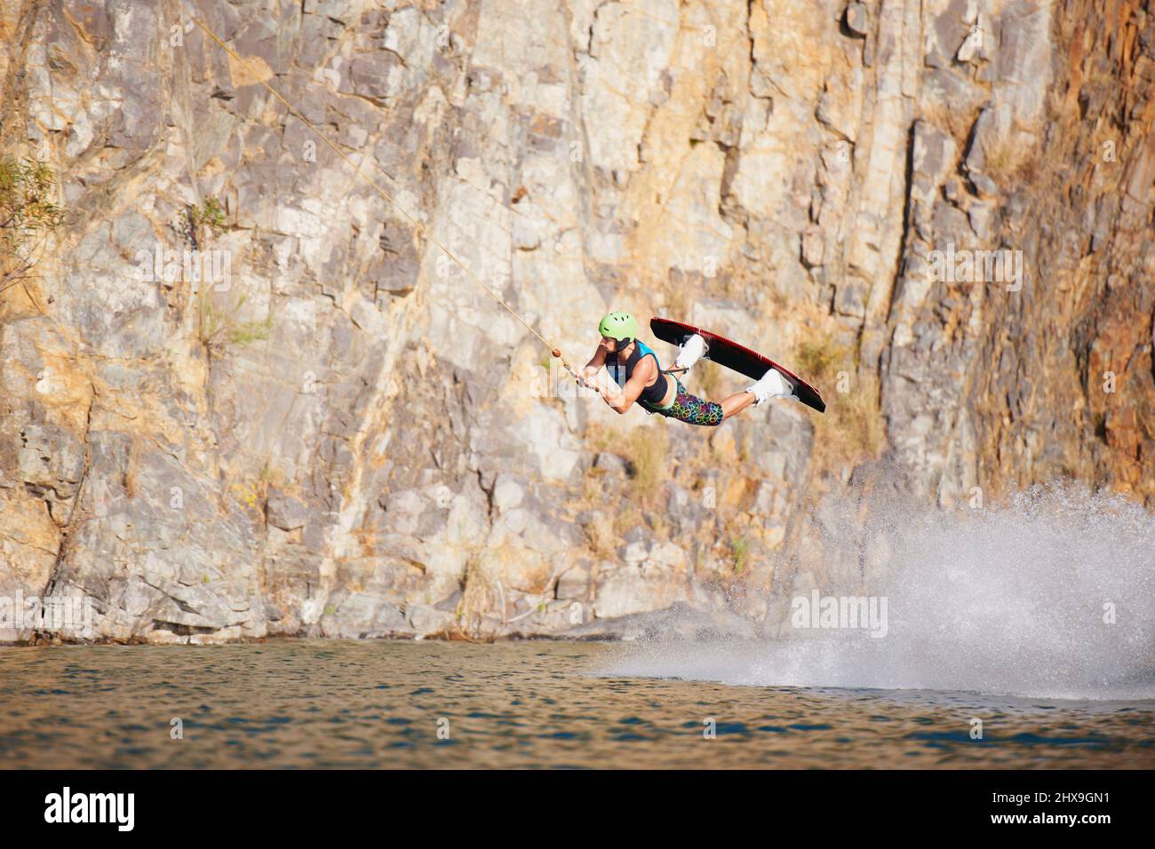 A Young Man Wearing A Helmut And Lifejacket Wakeboarding On A Lake A