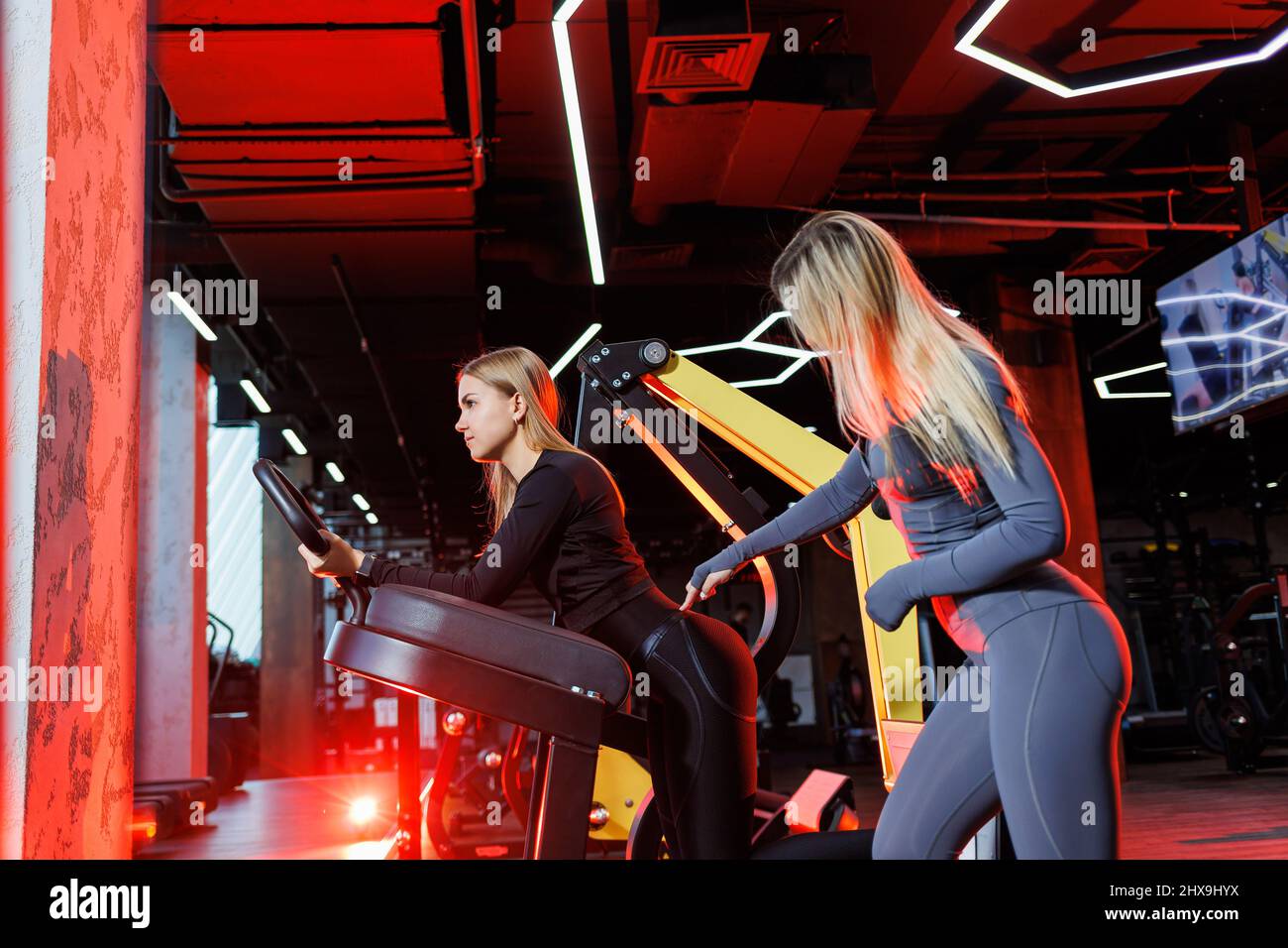 Young slender woman in the gym performs exercises under the guidance of ...