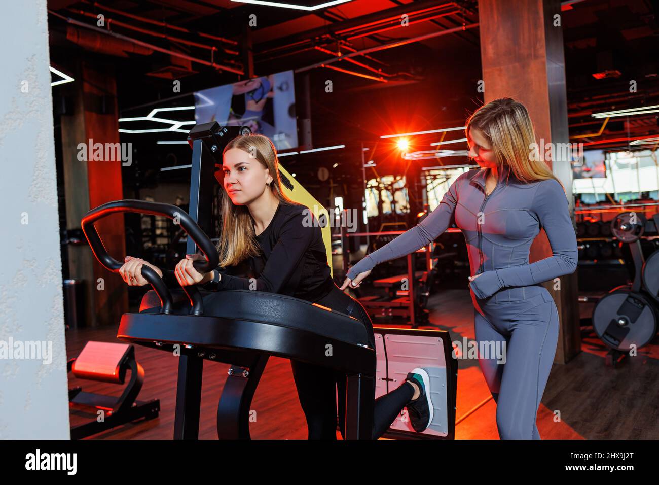 Young slender woman in the gym performs exercises under the guidance of ...