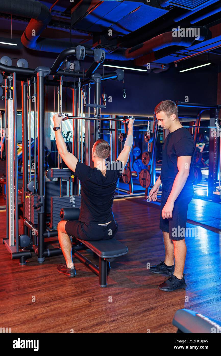 A young man performs exercises in the gym under the supervision of a ...