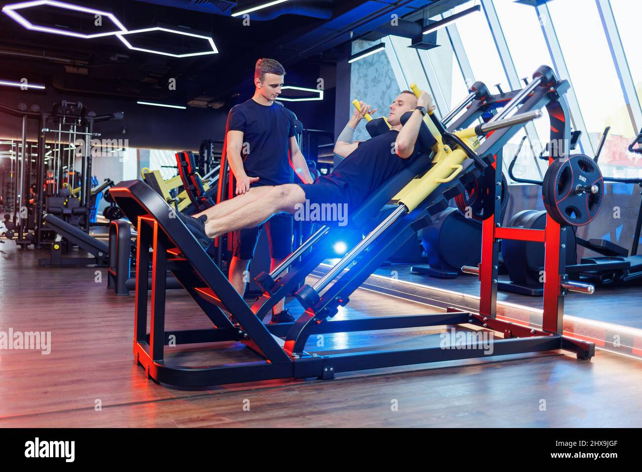 A strong young man performs exercises in the gym under the supervision ...