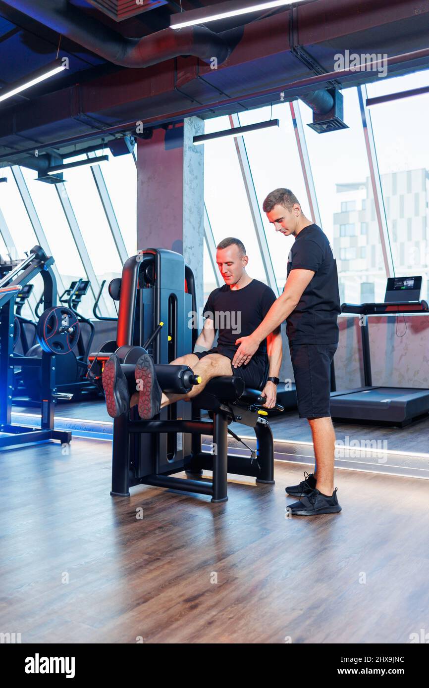 Athletic man doing exercises with the help of his personal trainer in a ...