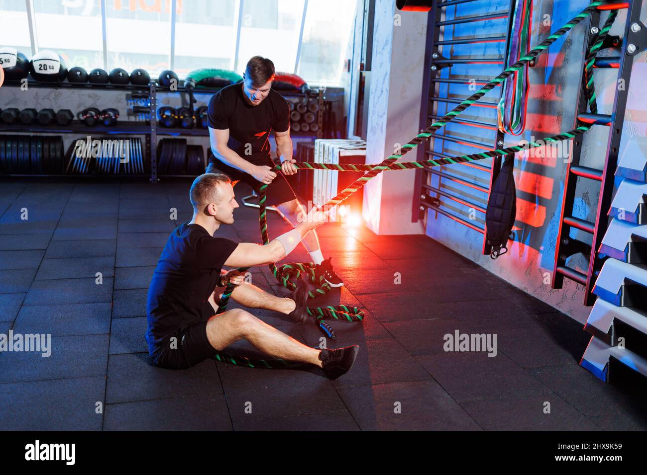 Athletic man doing exercises with the help of his personal trainer in a ...