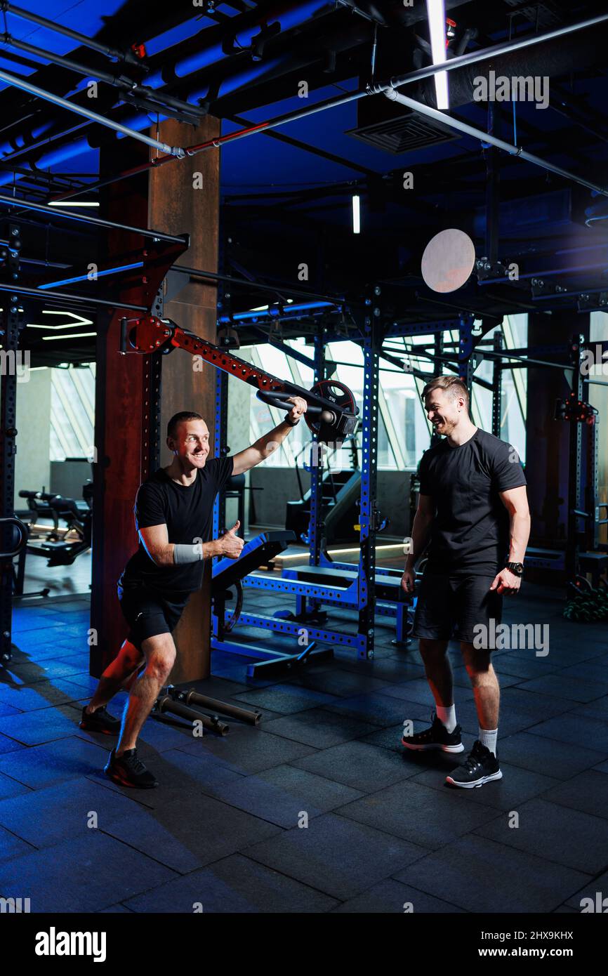 Athletic man doing exercises with the help of his personal trainer in a ...