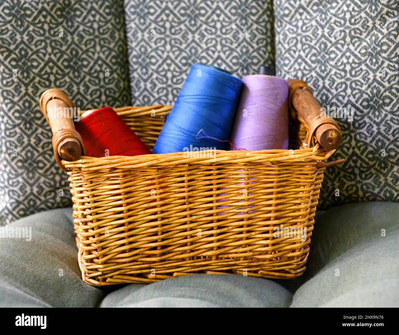 Wicker basket holds three spools of thread on spools. One is red blue ...