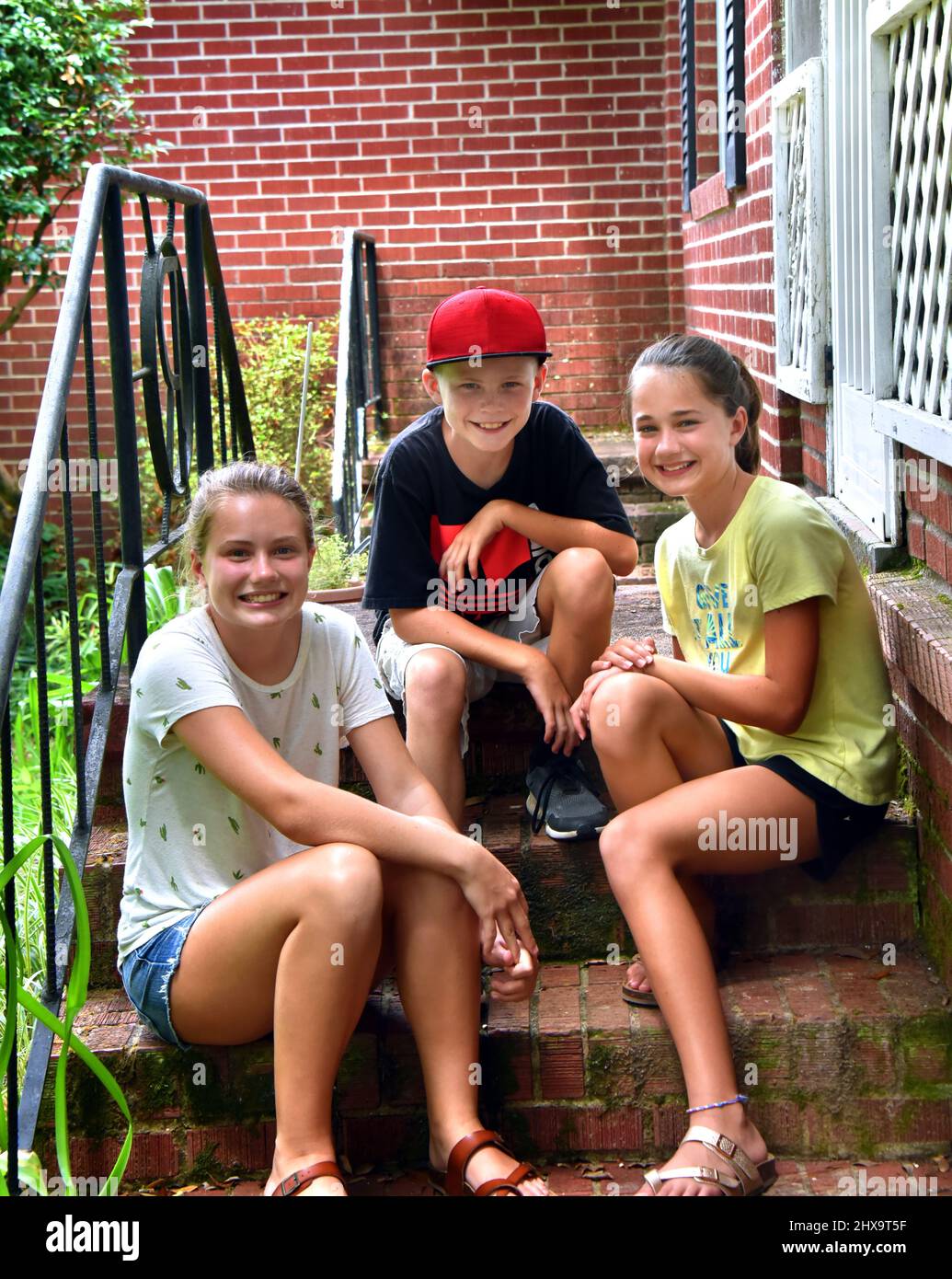 Three young people sit on the steps of their home. They are relaxed and ...