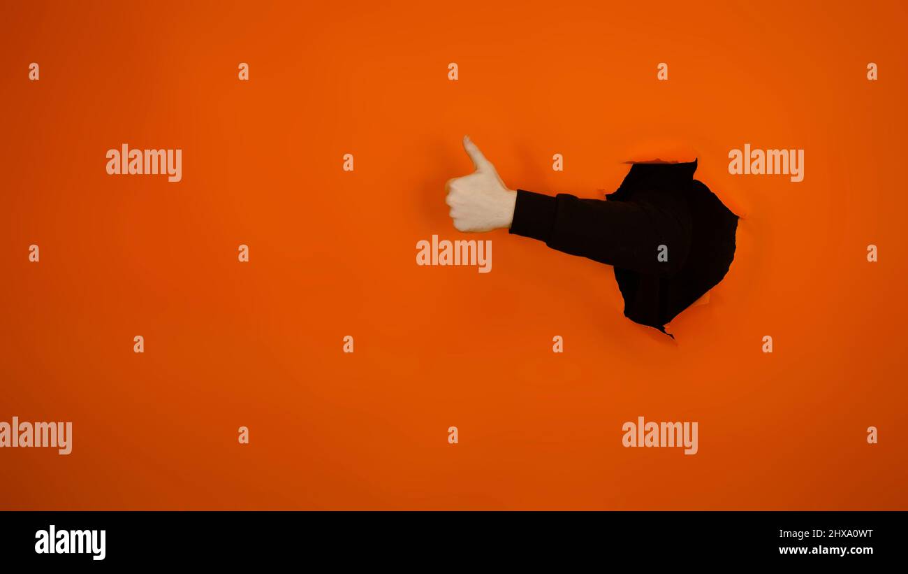 Man's hand showing thumb up and sticking out of hole of orange ...