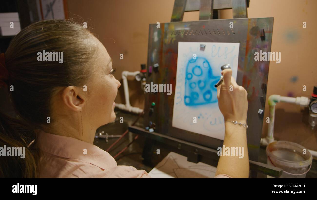 Woman artist learns to paint with airbrush with acrylic dye, paper and ...