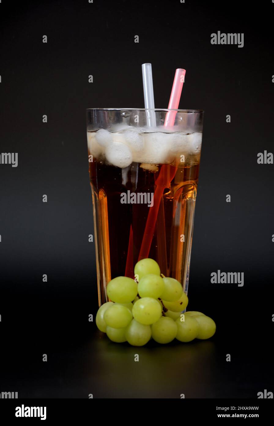 A tall glass of grape juice with ice and straws on a black background ...