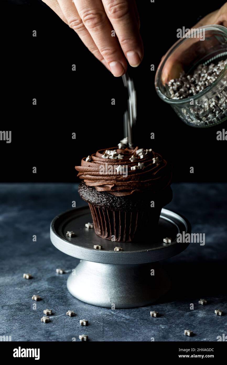 Decorating a chocolate cupcake with falling sprinkles blurred to depict ...
