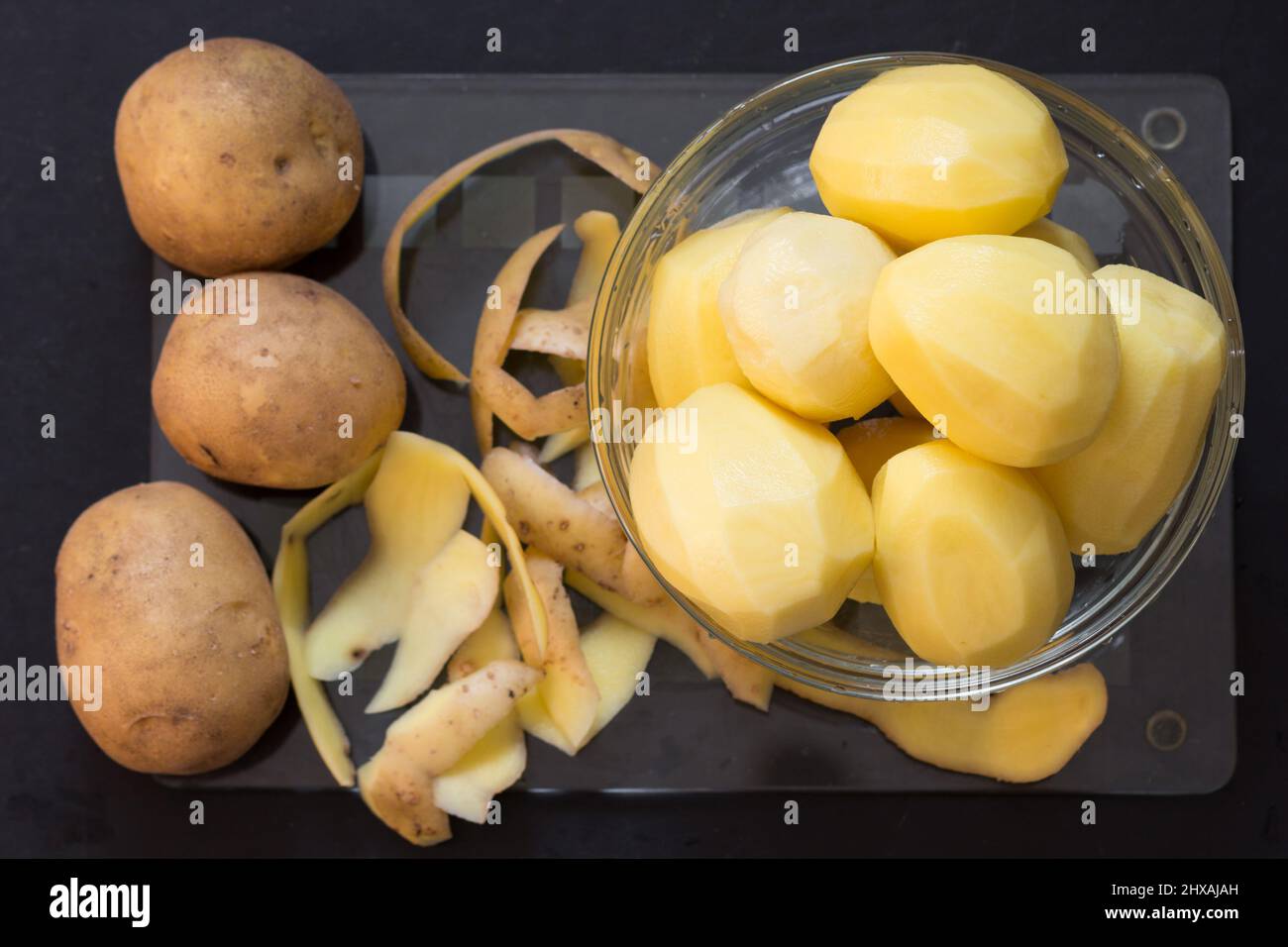 top view of raw unpeeled potato with peels and peeled potato in glass ...