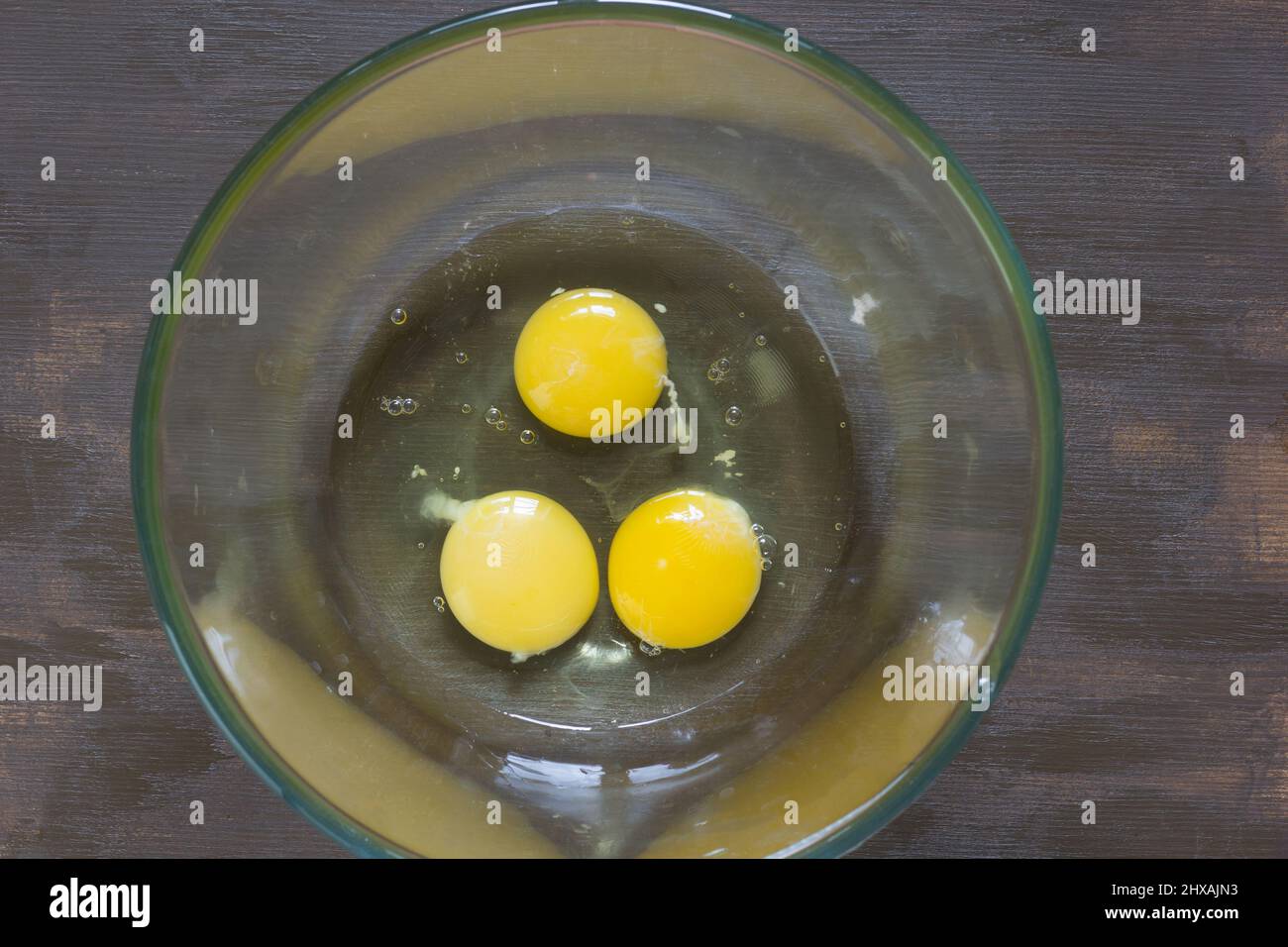 Three raw chicken yolks and whites in glass bowl on wooden table Stock ...