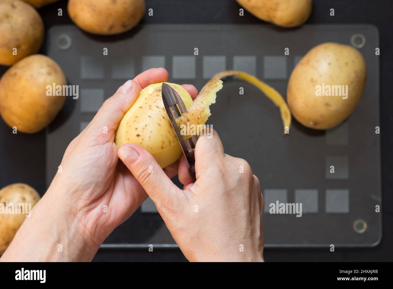 top view of woman hand peeling raw potato with peeler knife on the ...
