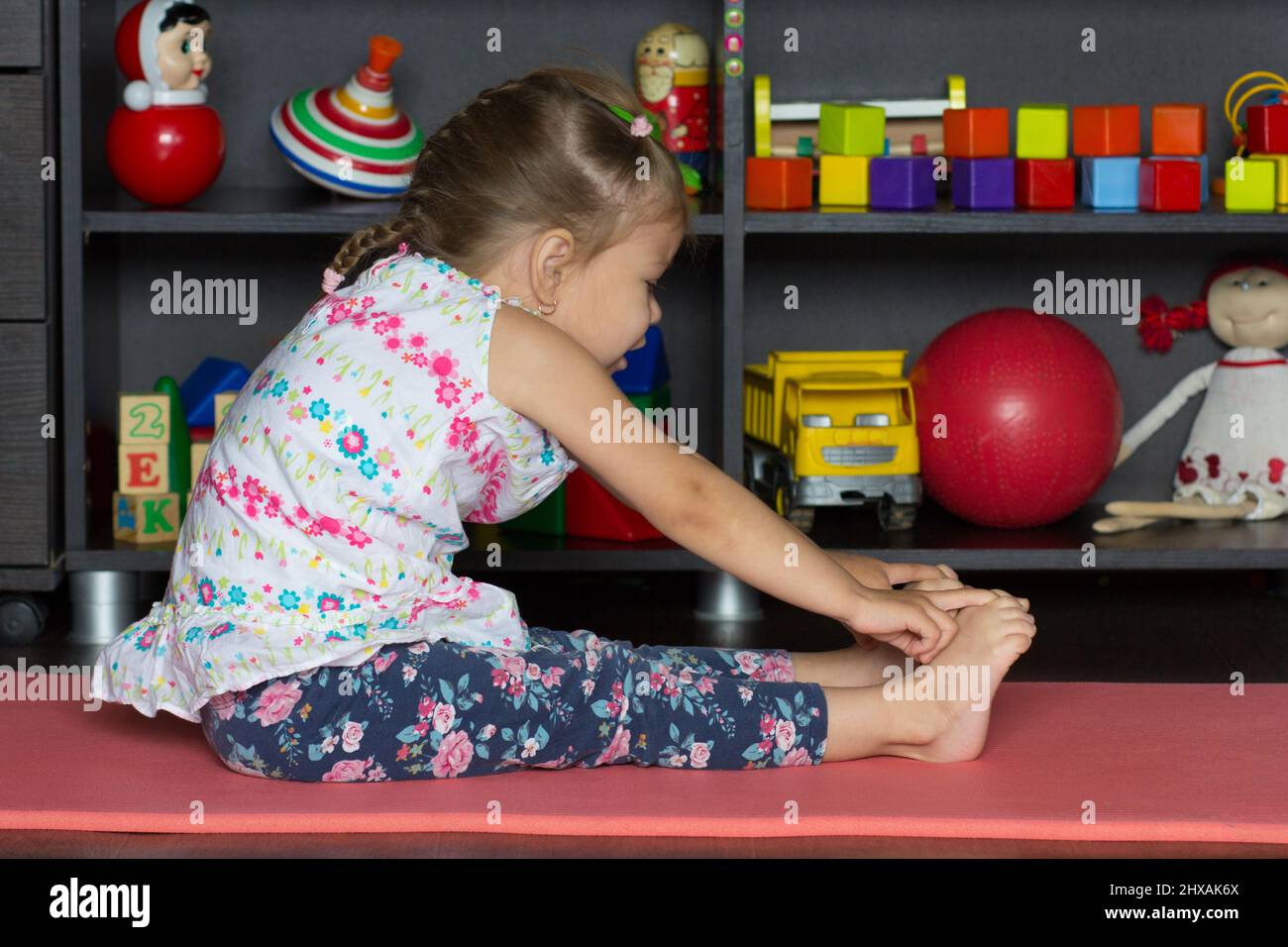 Child bending to her top of legs sitting on the matt Stock Photo - Alamy
