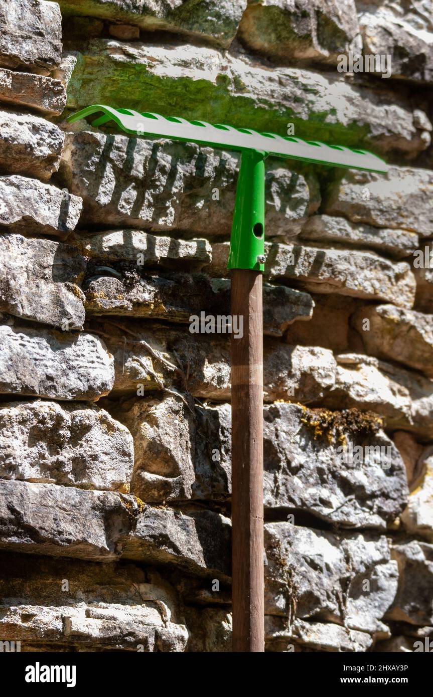 Green rake hanging from stone wall Stock Photo - Alamy