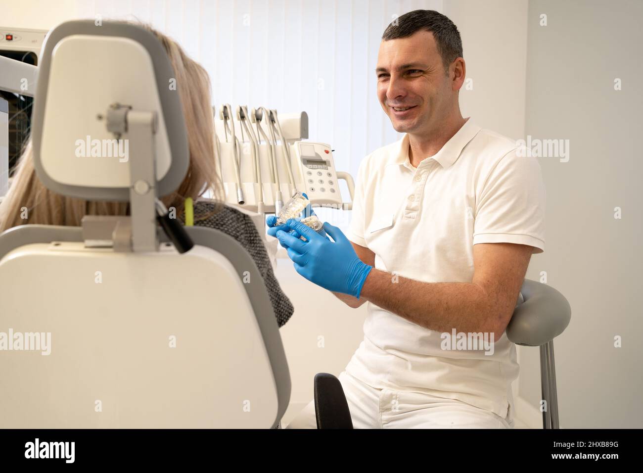 a man in a smock doctor dentist shows an artificial plastic jaw bite ...