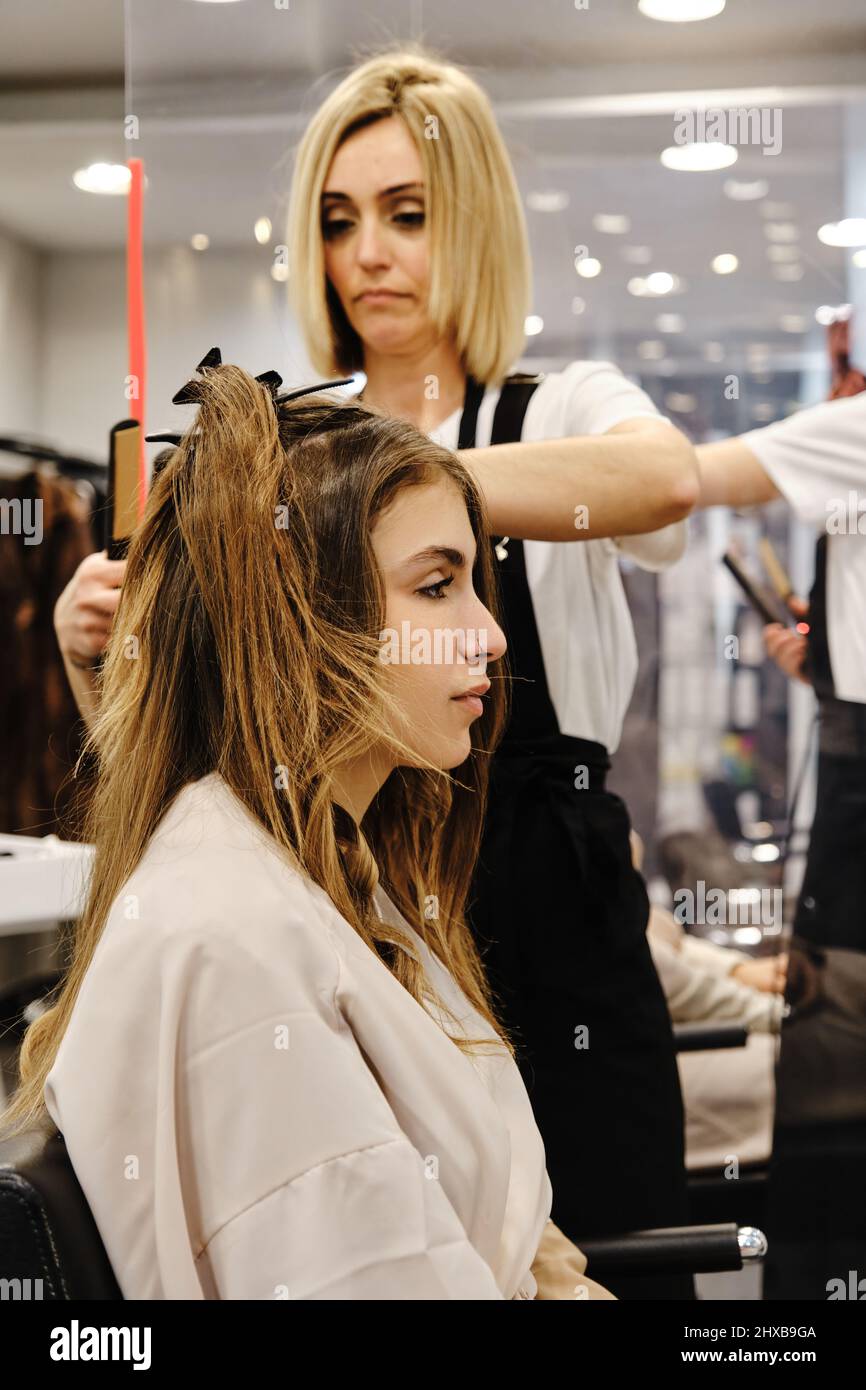 Professional stylist straightening the client hair while making her a ...