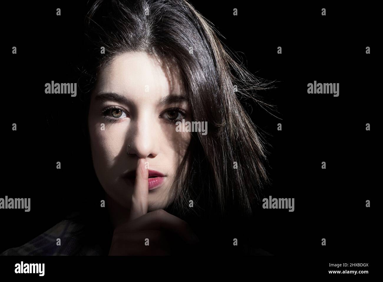 brunette woman commanding silence on black background Stock Photo - Alamy