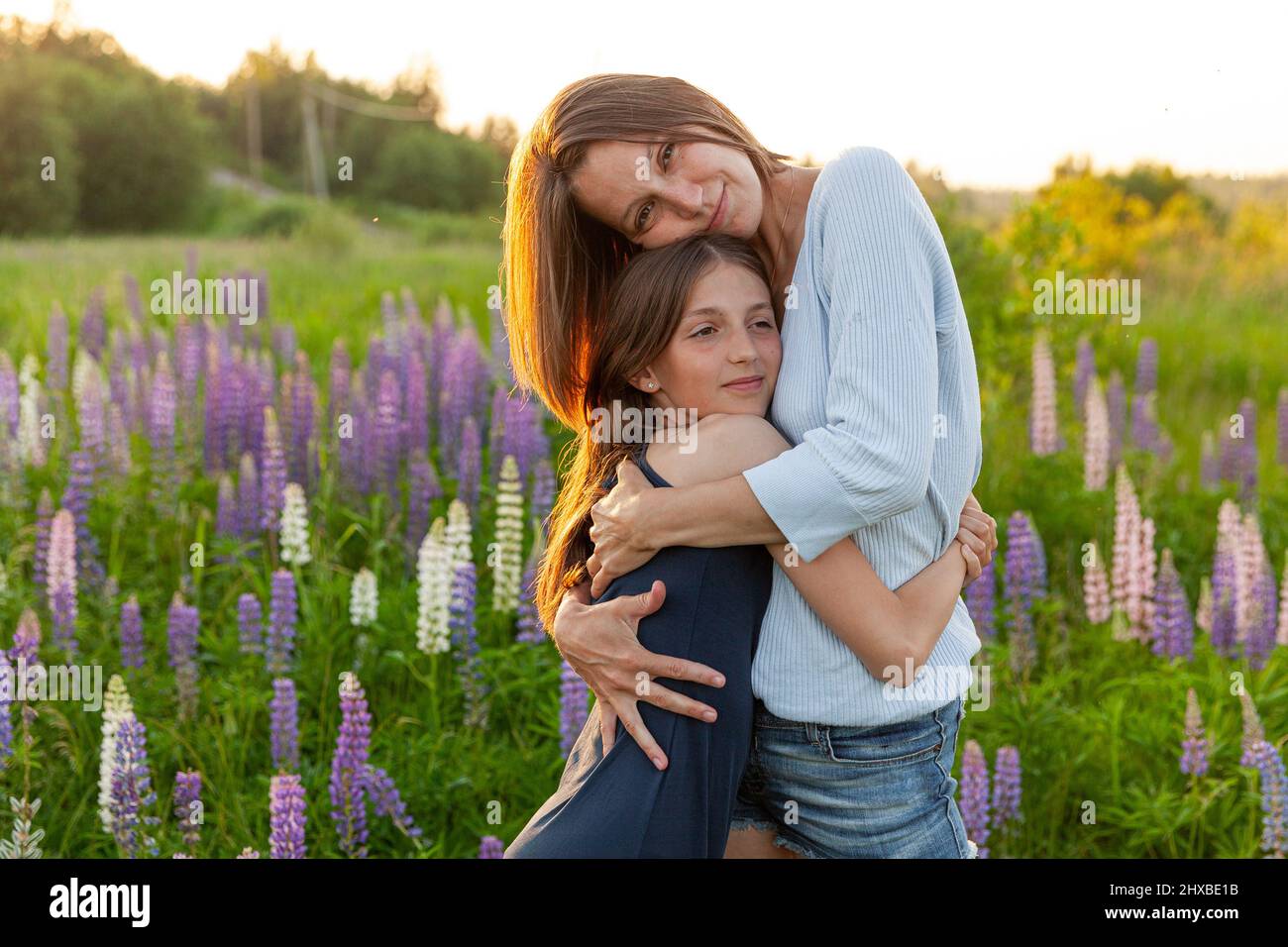 Young mother embracing her child outdoor. Woman and teenage girl on summer field with blooming ...