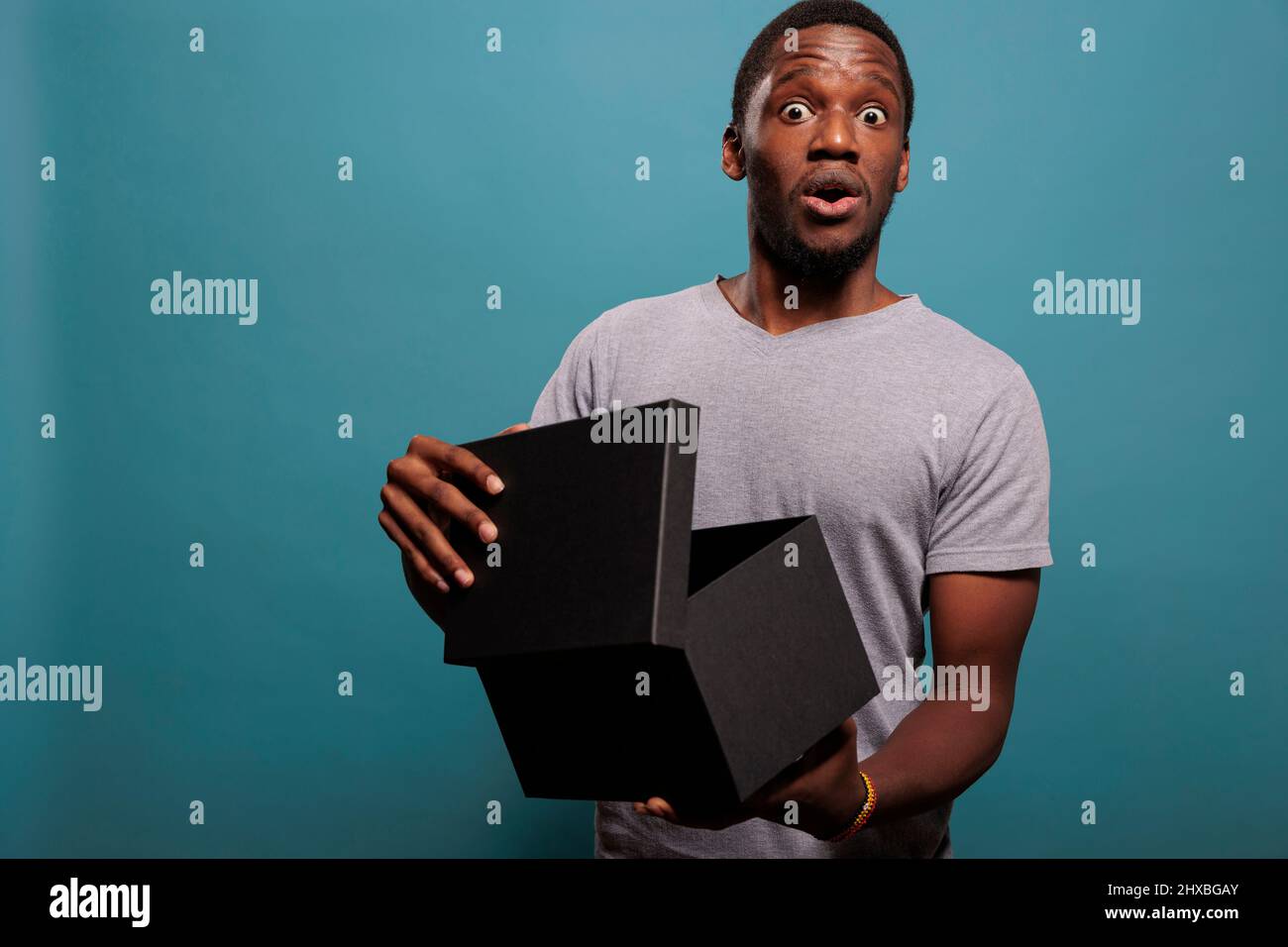 Cheerful guy feeling surprised after unpacking gift box and opening to ...