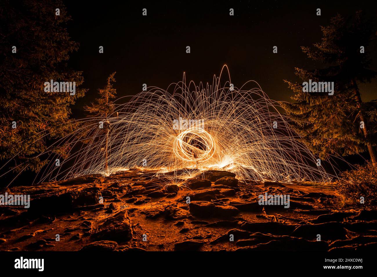 Golden sparks spray at night at stones rocks puddle reflects the sparks ...