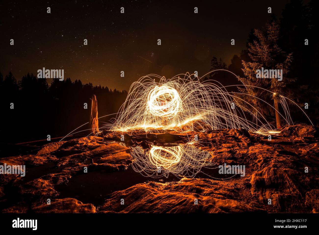 Golden sparks spray at night at stones rocks puddle reflects the sparks ...