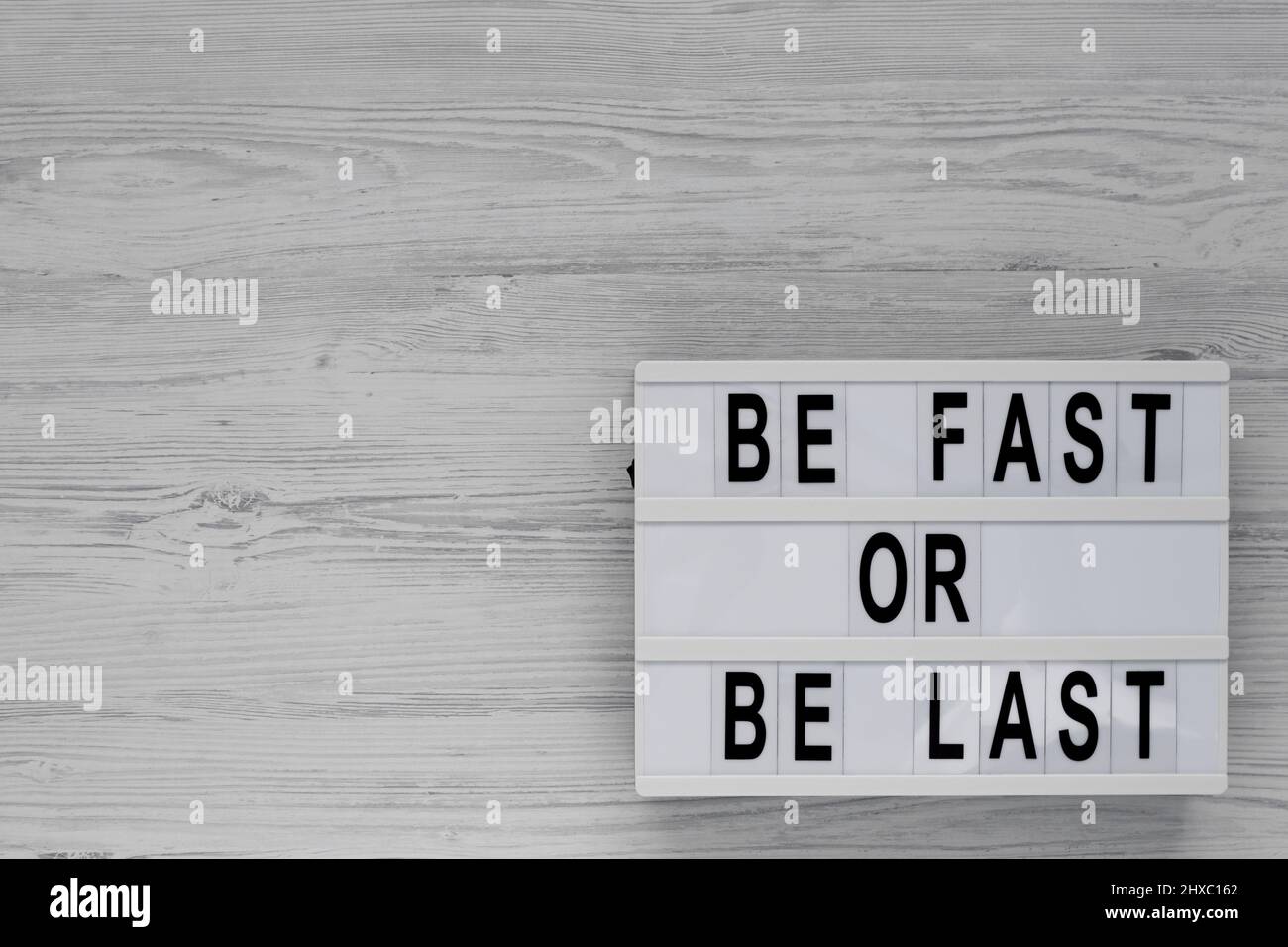 'Be Fast or Be Last' on a lightbox on a white wooden background, top view. Flat lay, overhead ...