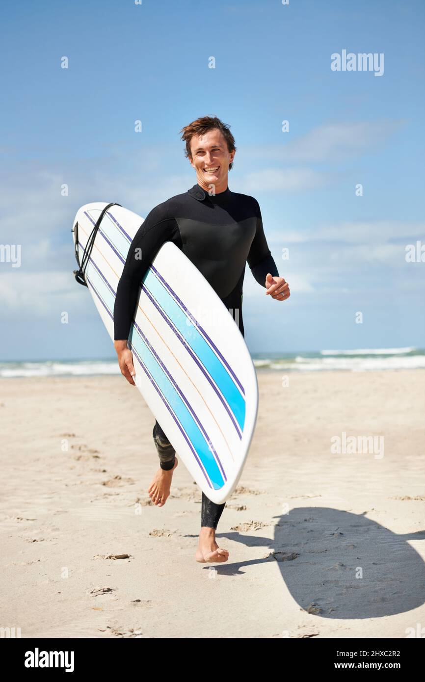 Surf spirit. A handsome surfer running down the beach with his ...
