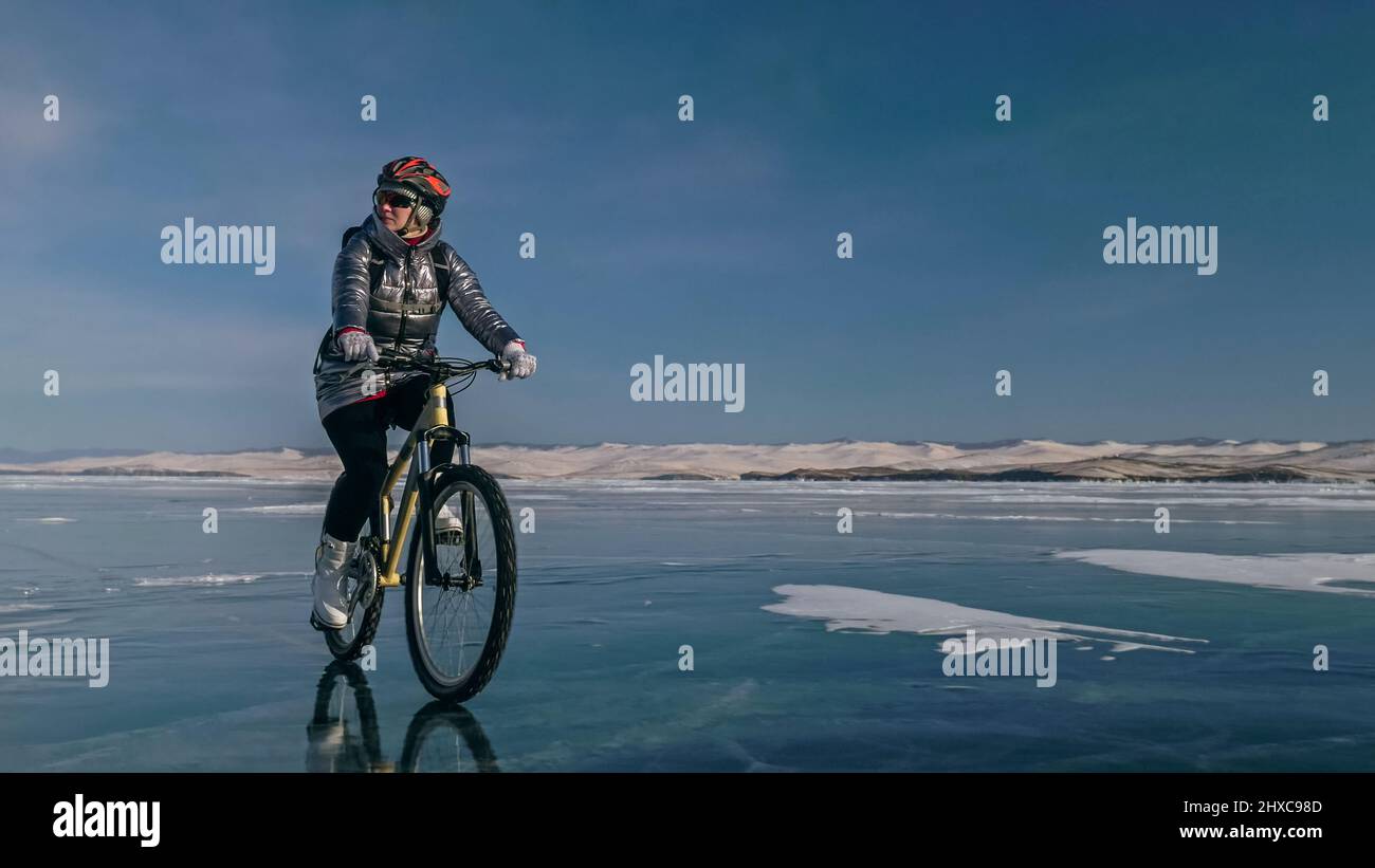 Woman is riding bicycle on the ice. Girl is dressed in a silvery down ...