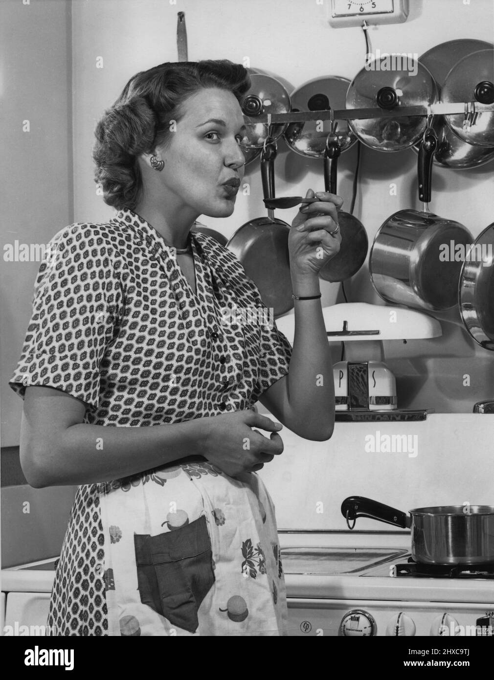 Mid-30's woman in dress and apron, taste testing her cooking Stock ...