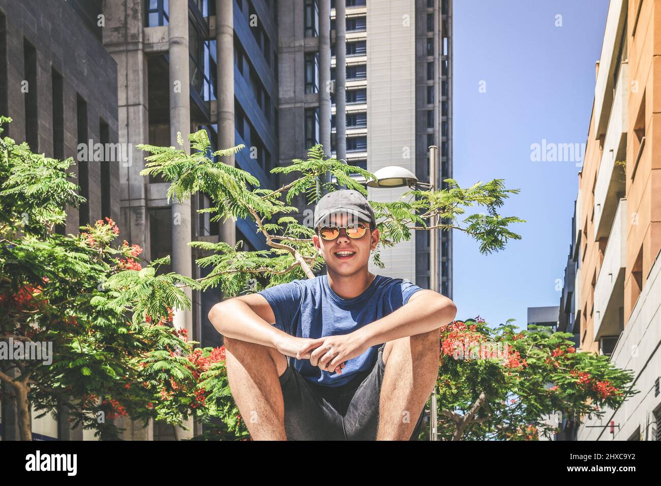 Smiling young boy taking rest sitting in the city, trees and palaces in ...