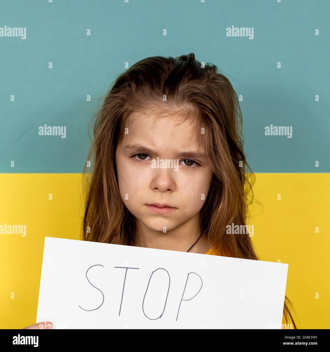 The face of a crying girl close-up. A girl holds a STOP poster in her ...
