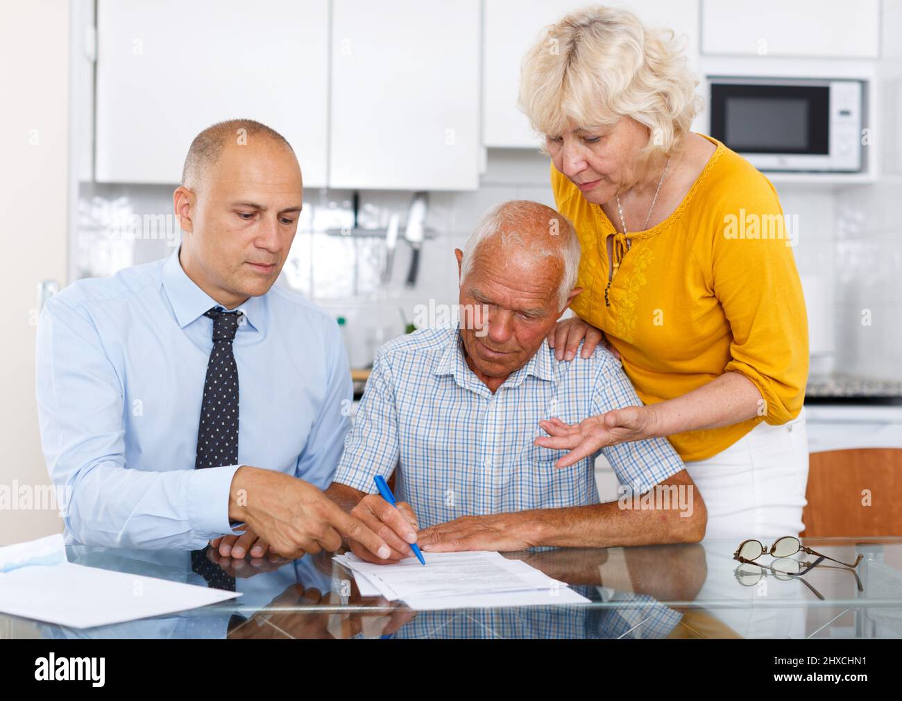 Elderly husband and wife signing agreement papers with bank worker ...