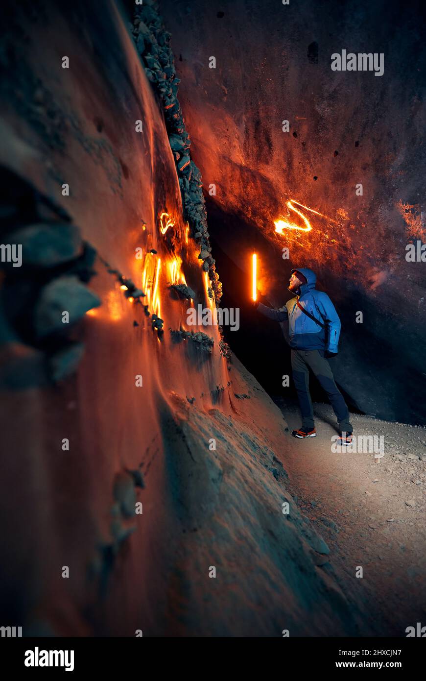 Tourist man holding red glow lamp in deep narrow glacial ice cave with ...