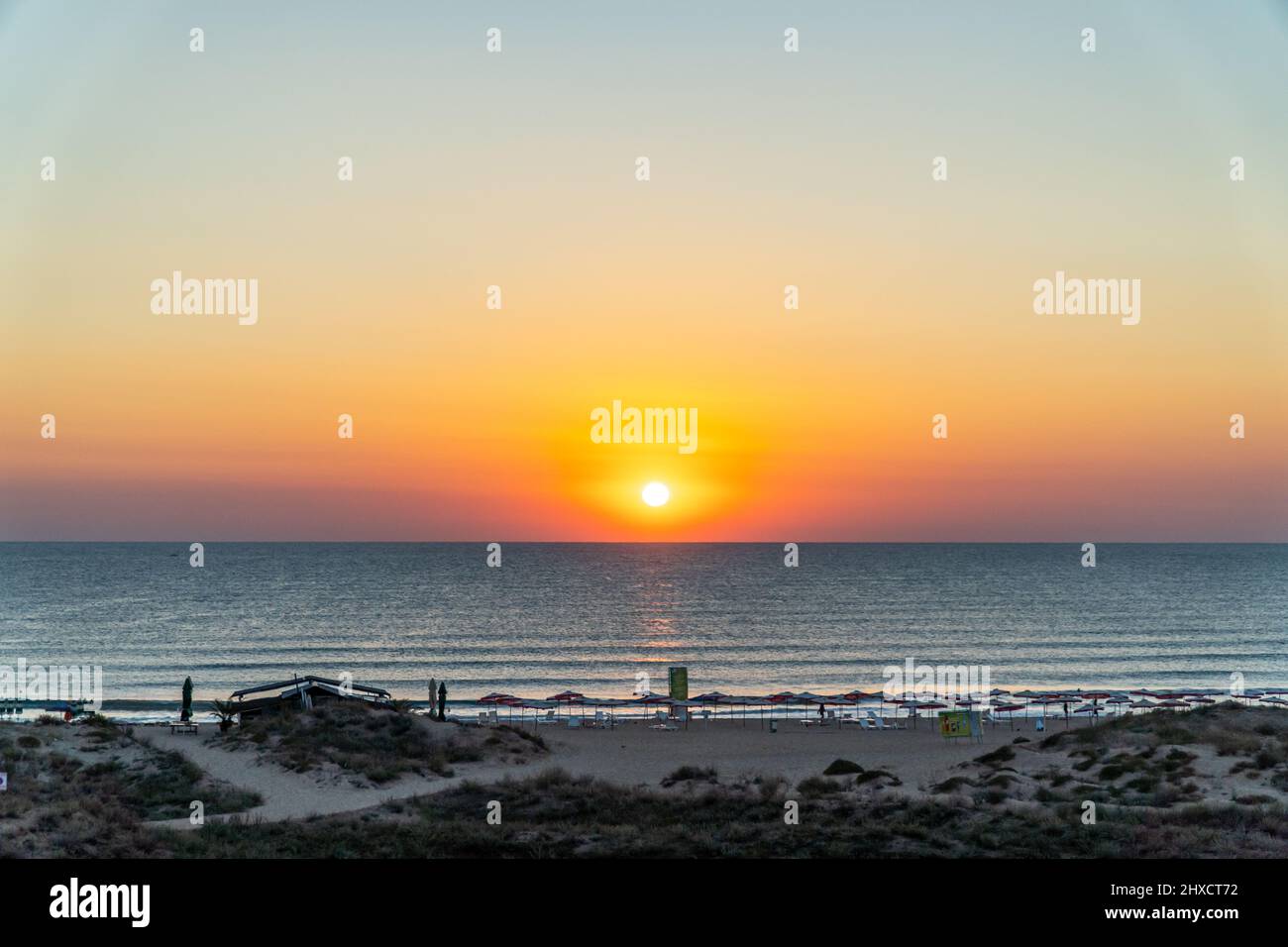 Amazing sunrise over the sand dunes on the shore with sun beds and ...