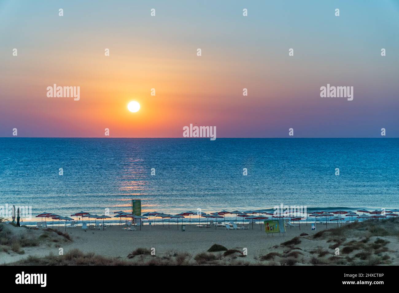Amazing sunrise over the sand dunes on the shore with sun beds and ...