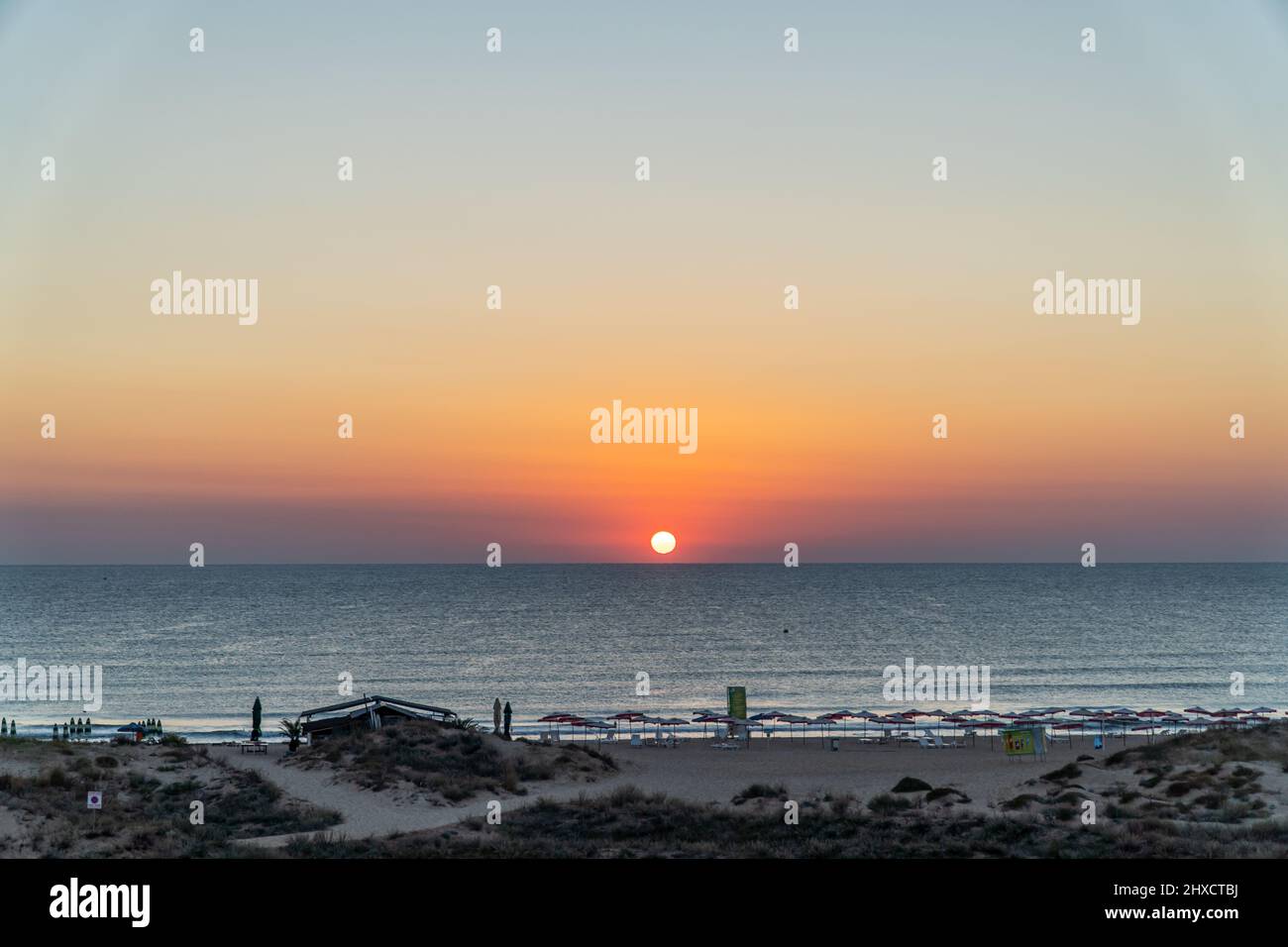 Amazing sunrise over the sand dunes on the shore with sun beds and ...