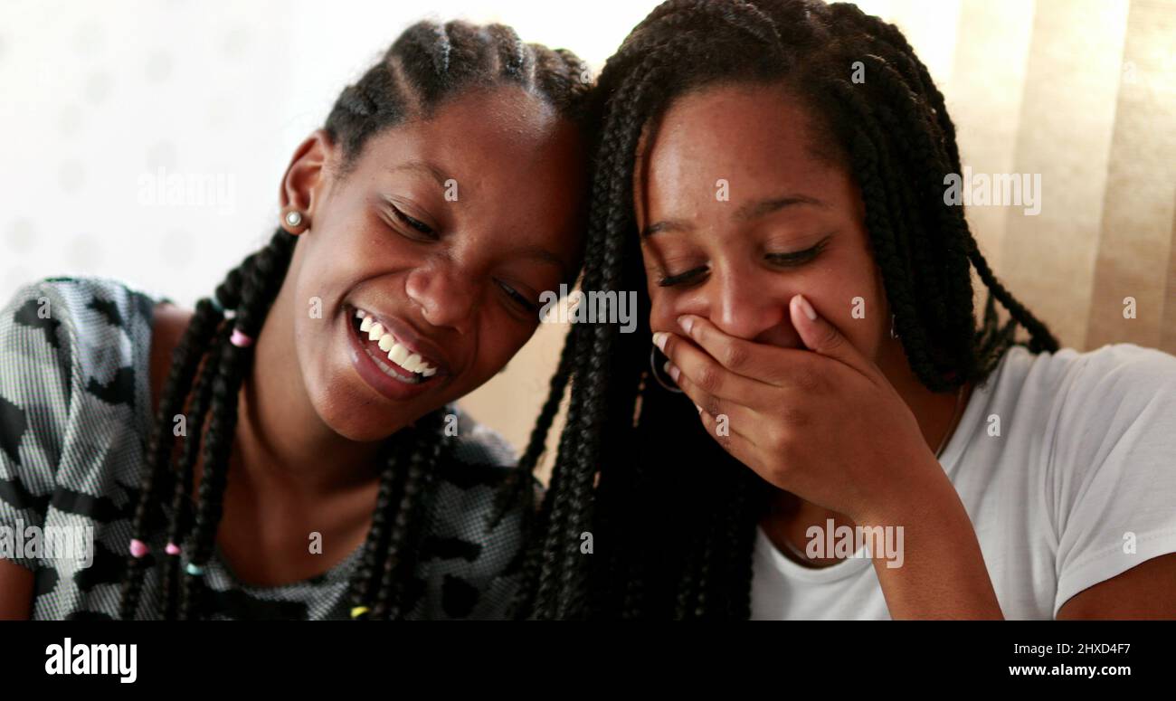 Girlfriend sharing cellphone screen. Black sisters laughing together, girls covering hands with ...