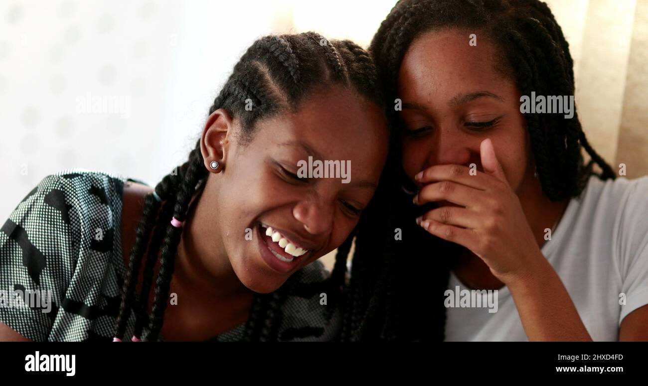 Girlfriend sharing cellphone screen. Black sisters laughing together, girls covering hands with ...