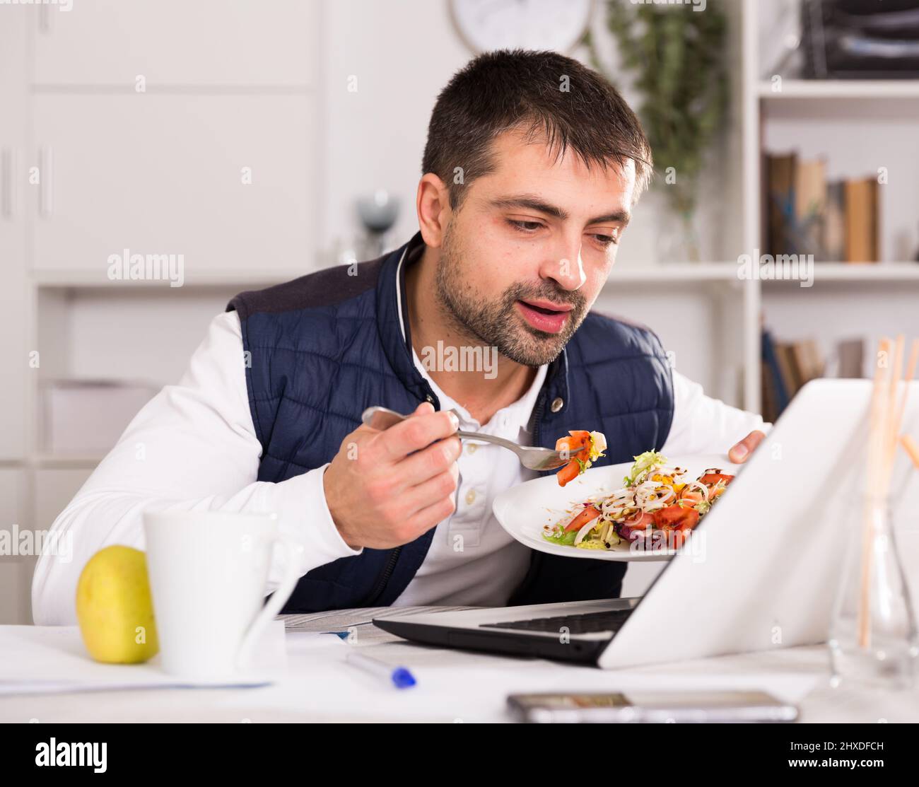 Portrait of man eating vegetable salad at table with laptop Stock Photo ...