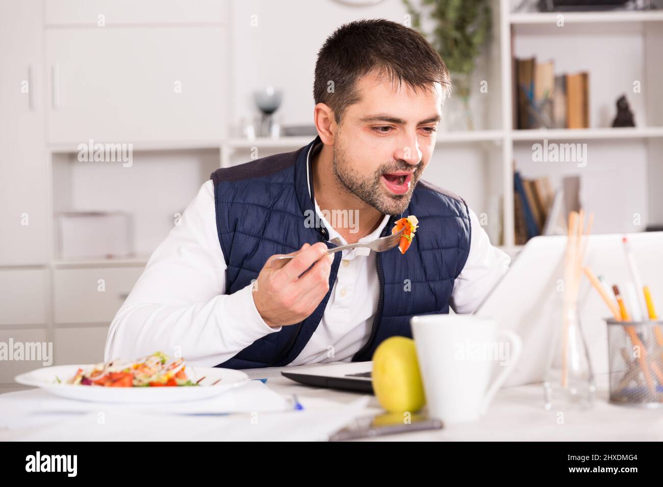 Positive young male holding fork, eating vegetable salad Stock Photo ...